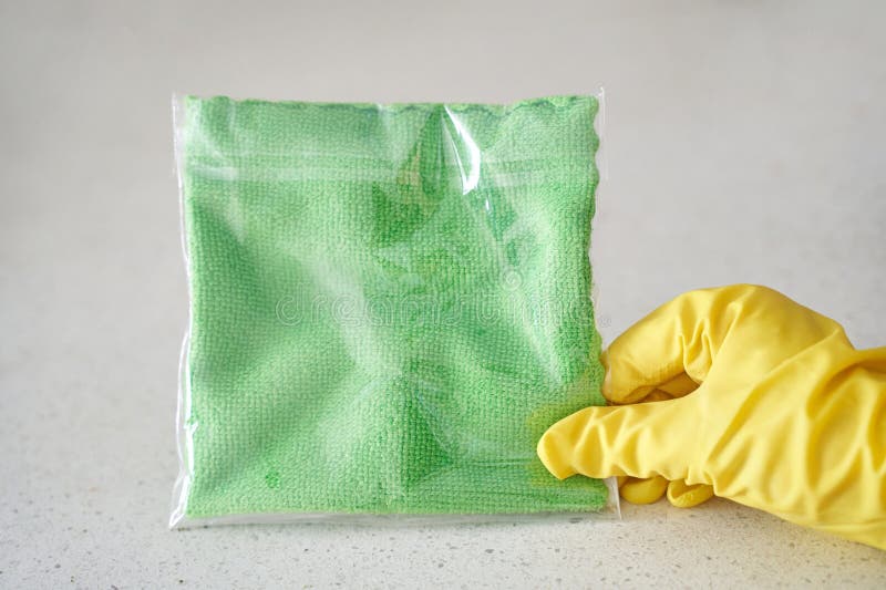 Yellow Gloved Hand Holding Green Cleaning Cloth in Plastic Bag on Light ...