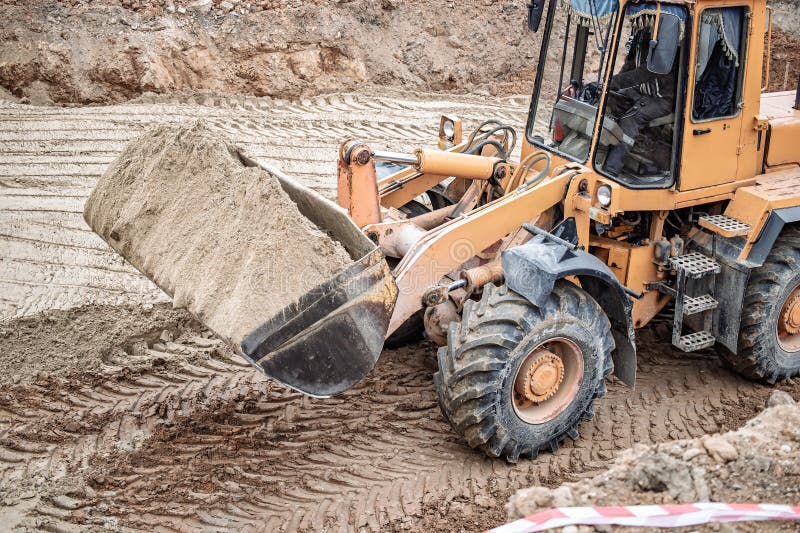 A Construction Site Worker Operates a Yellow Loader As it Lifts Sand ...