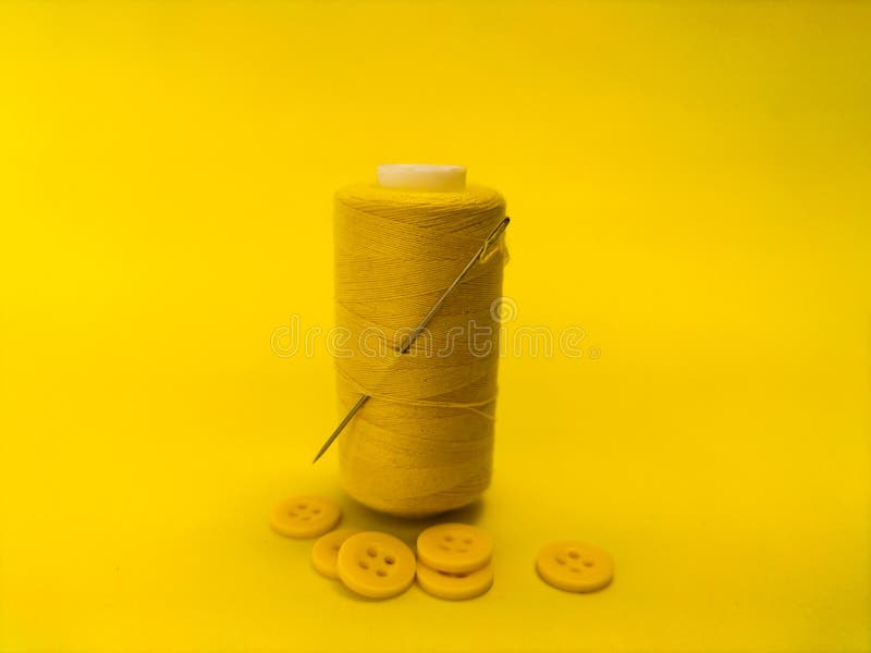 Yellow Sewing Thread Spool with a Needle and Buttons Placed on Yellow ...
