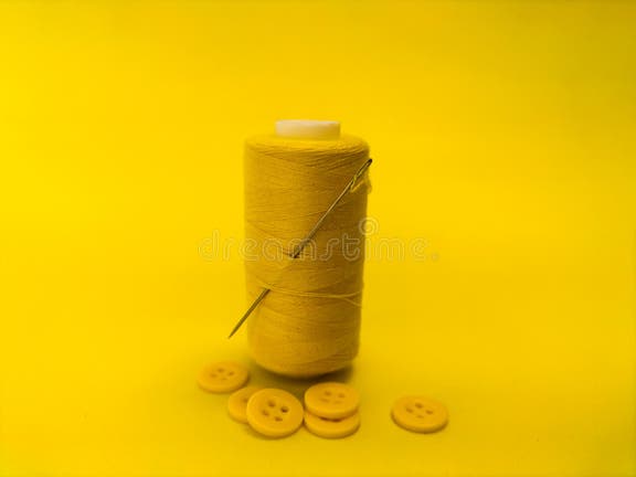 Yellow Sewing Thread Spool with a Needle and Buttons Placed on Yellow ...