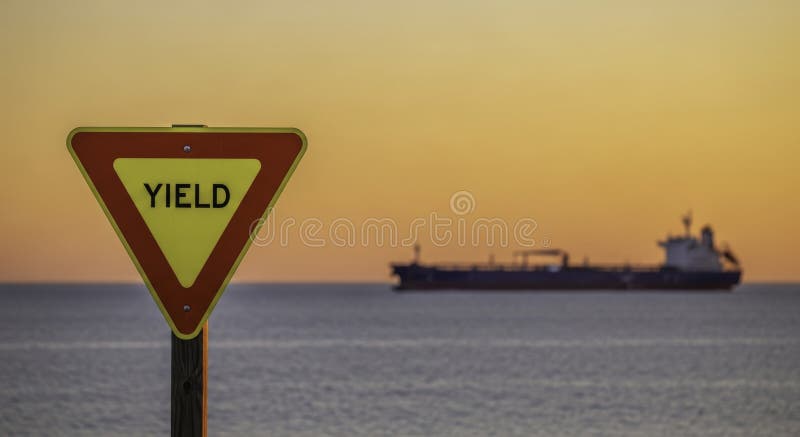 Yellow Yield Sign on Pole with Distant Ship on Ocean at Golden Sunset ...