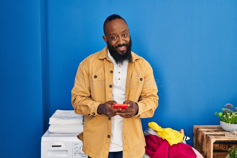 Young African American Man Using Smartphone Waiting for Washing Machine ...