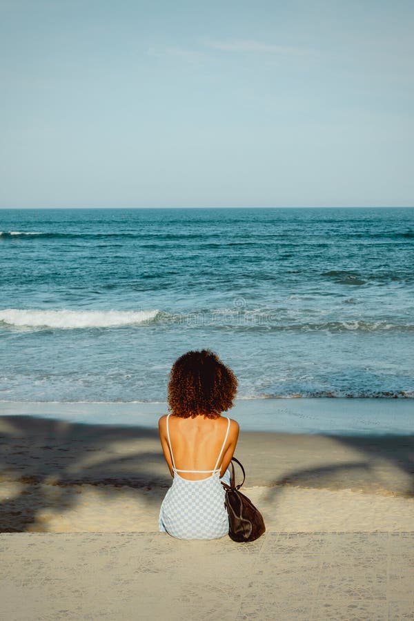 Young African Female Sitting on Beach Looking at Ocean Waves Stock ...