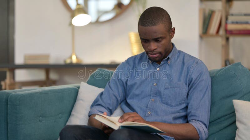 Young African Man Reading Book on Sofa Stock Photo - Image of read ...