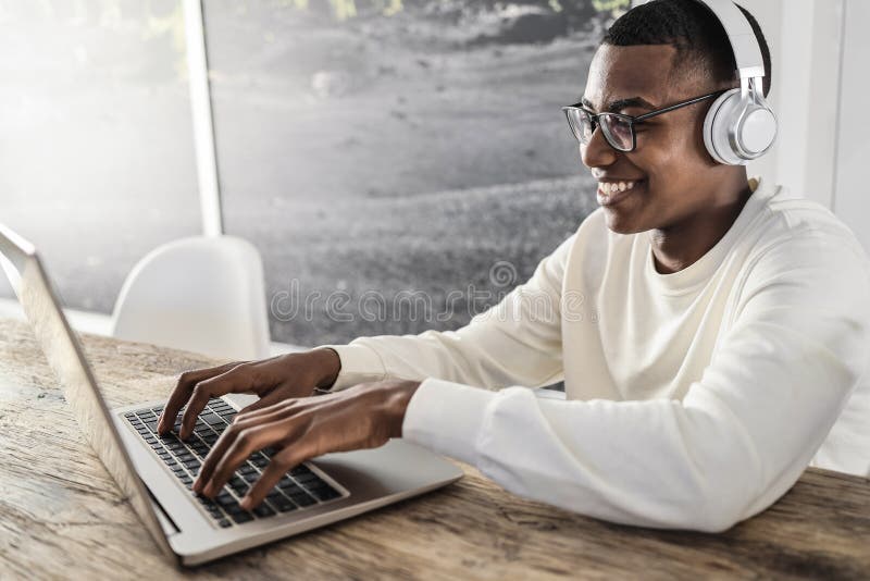 Young African Man Using Laptop Computer while Wearing Headphones at ...