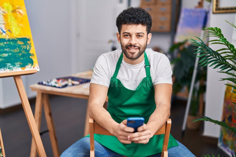 Young Arab Man Artist Using Smartphone Sitting on Chair at Art Studio ...
