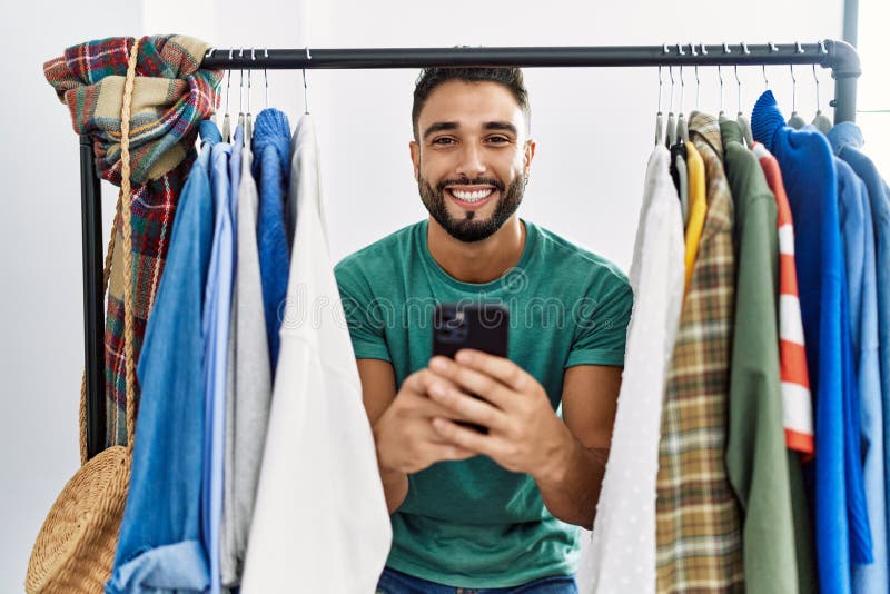 Young Arab Man Customer Using Smartphone Appearing through Clothes Rack ...