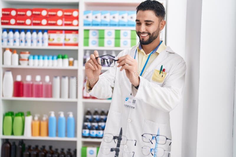 Young Arab Man Pharmacist Smiling Confident Holding Glasses at Pharmacy ...