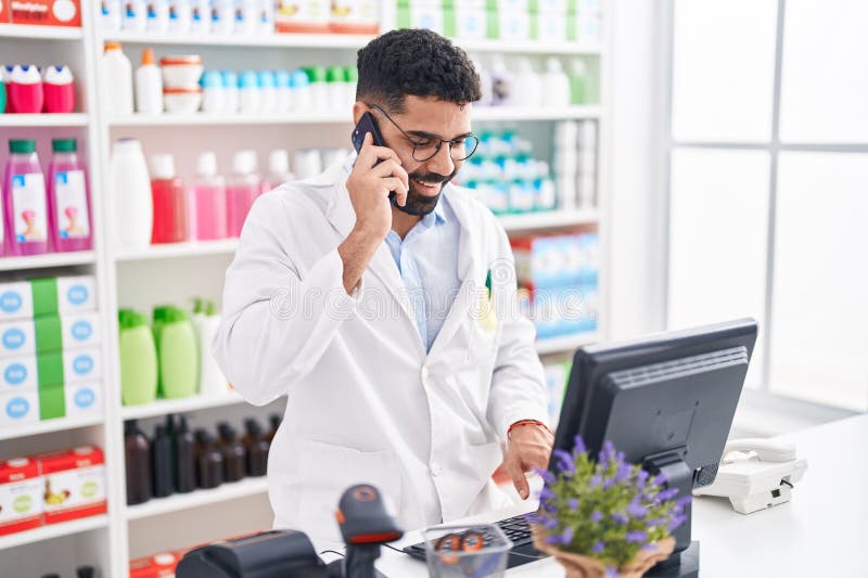 Young Arab Man Pharmacist Talking on Smartphone Using Computer at ...