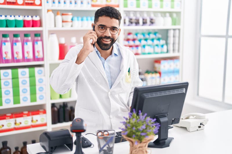 Young Arab Man Pharmacist Talking on Smartphone Using Computer at ...