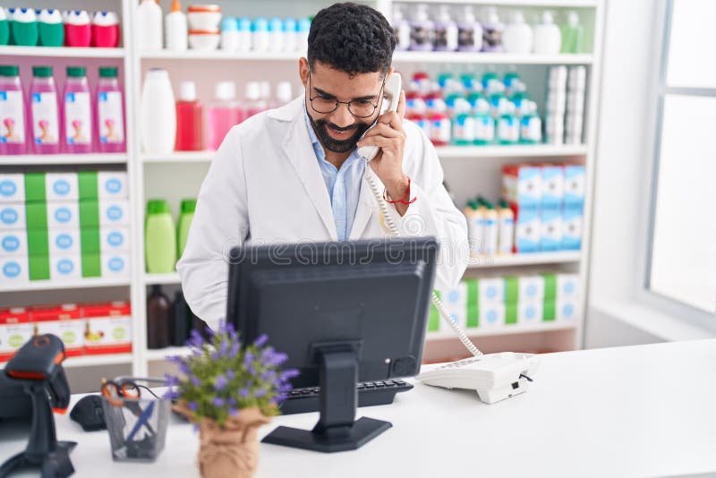 Young Arab Man Pharmacist Talking on Telephone Using Computer at ...