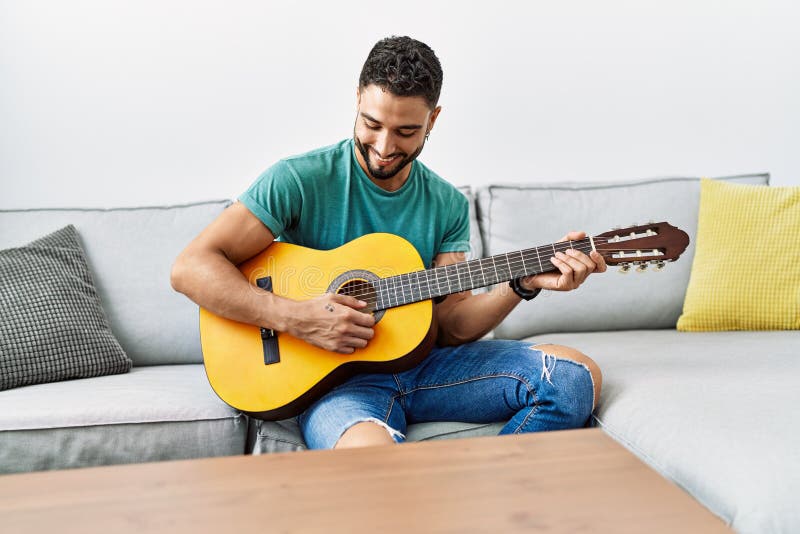 Young Arab Man Playing Classical Guitar Sitting on Sofa at Home Stock ...