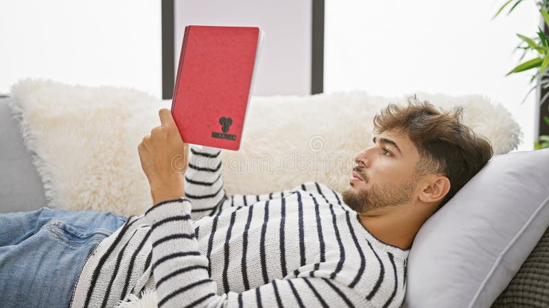 Young Arab Man Reading Book Lying on Sofa at Home Stock Image - Image ...