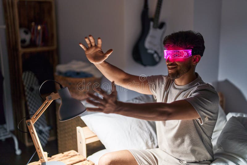 Young Arab Man Using Augmented Reality Glasses Sitting on Bed at ...