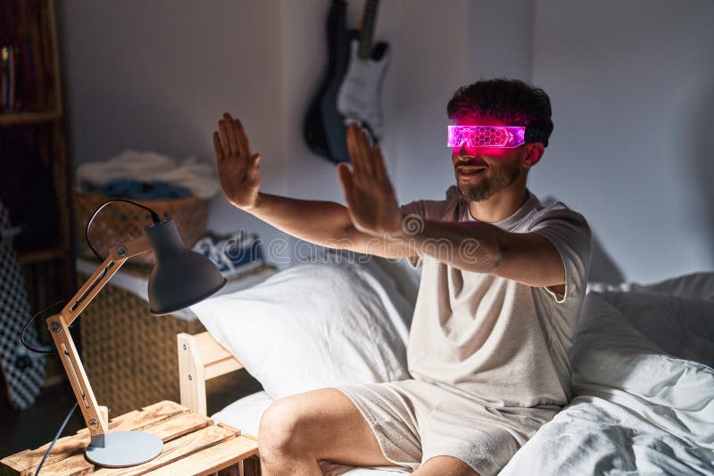 Young Arab Man Using Augmented Reality Glasses Sitting on Bed at ... Young Arab Man Using Augmented Reality Glasses Sitting on Bed at ...
