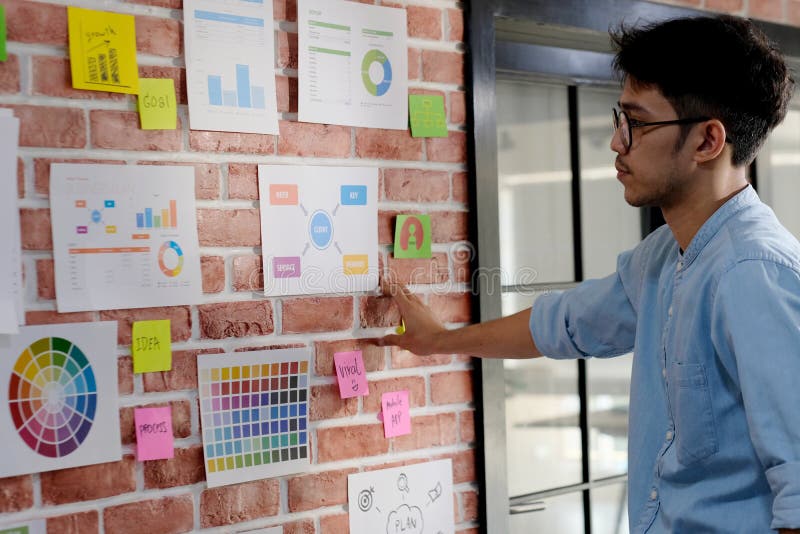 Young Asian Creative Man Reading and Thinking about Paper Work Ideas on ...