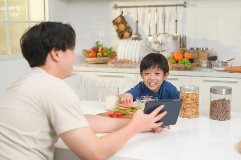 Young Asian Father and His Son Using Digital Tablet Enjoying Together in Kitchen at Home Stock ...