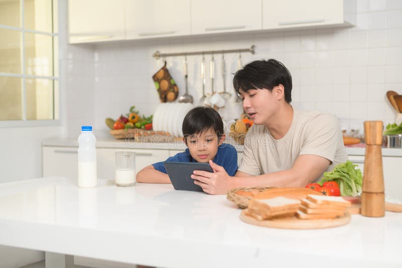 Young Asian Father and His Son Using Digital Tablet Enjoying Together in Kitchen at Home Stock ...
