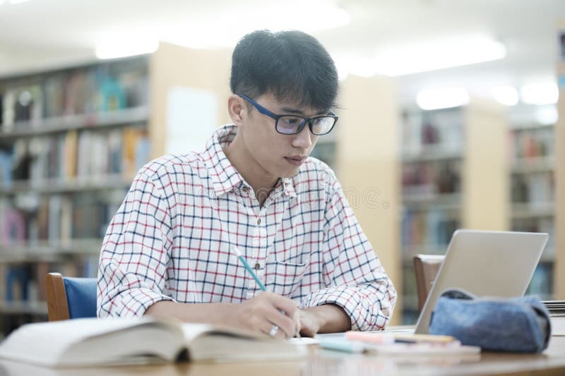 Young Asian Male Sitting Inside a Library Alone Doing Research. Man ...