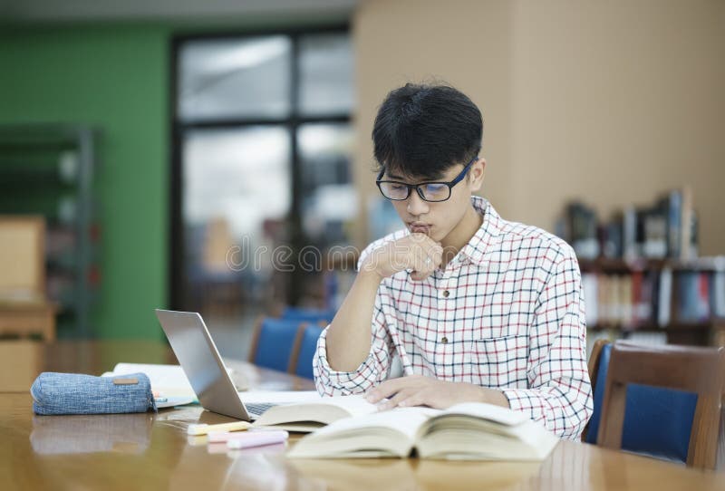 Young Asian Male Sitting Inside a Library Alone Doing Research. Man ...