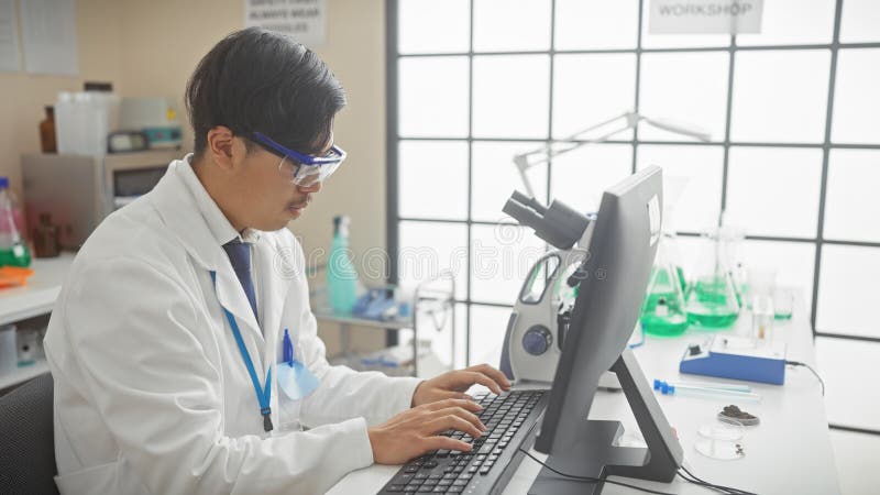 A Young Asian Man in a Lab Coat Working on a Computer in a Bright ...