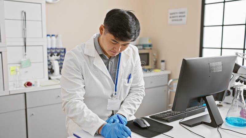 A Young Asian Man in a Lab Coat Works Diligently in a Modern Laboratory ...