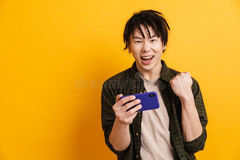 Young Asian Man Making Winner Gesture while Using Mobile Phone Stock ...