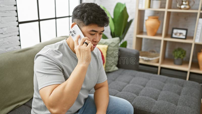 A Young Asian Man on a Phone Call in a Modern Living Room Setting Stock ...