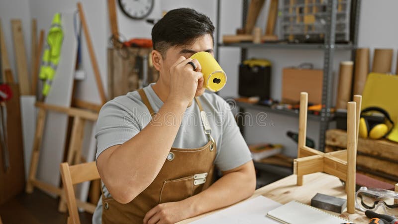 A Young Asian Man in a Workshop Drinks Coffee during a Break from ...