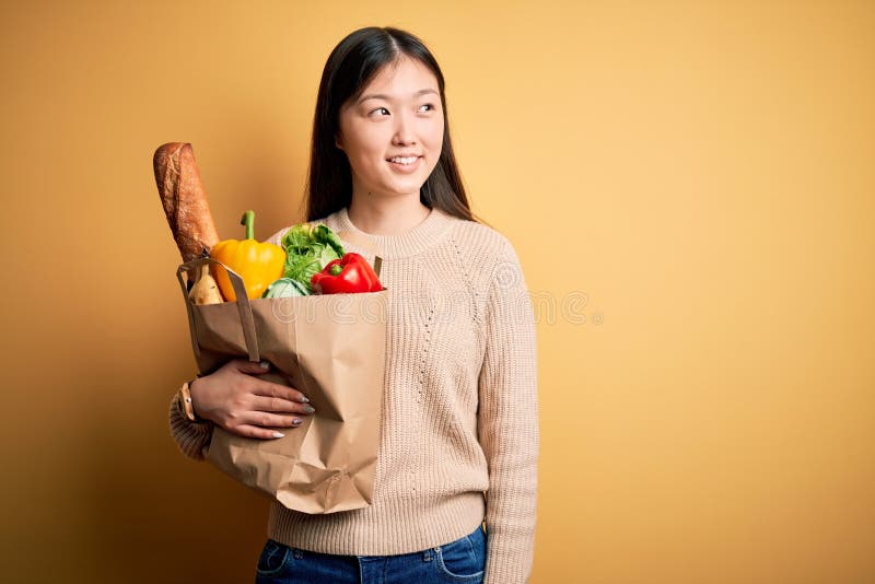 Young Asian Woman Holding Paper Bag Of Fresh Healthy Groceries Over
