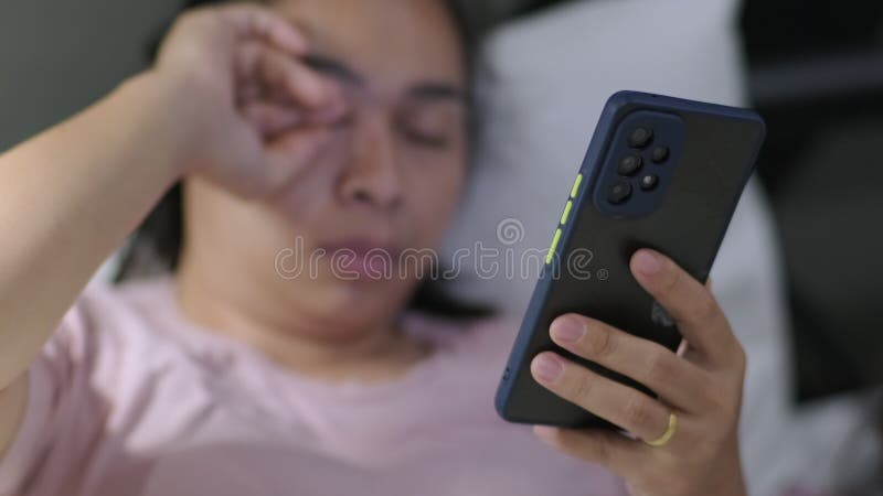 Young Asian Woman Lying On White Bed And Playing Smartphone At Night