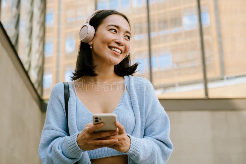 Young Smiling Asian Woman Using Cellphone while Standing Indoors Stock ... Young Smiling Asian Woman Using Cellphone while Standing Indoors Stock ...