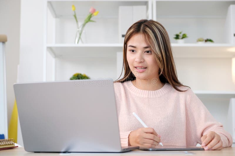 Young Asian Woman Writing on Digital Tablet while Looking at Laptop ...
