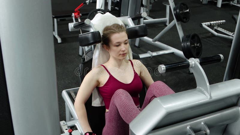 A Young, Athletic Woman Does a Leg Press on a Machine in the Gym, an ...