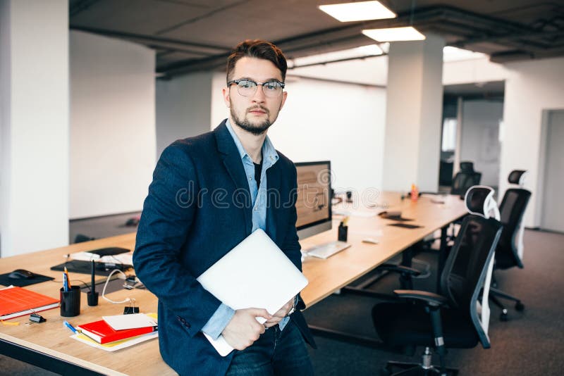 Young Attractive Man In Glassess Is Standing Near The Workplace In