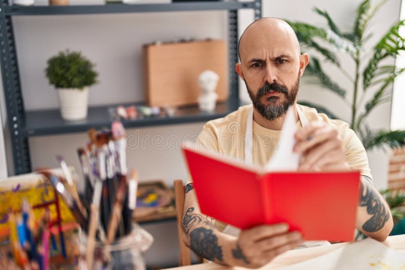 Young Bald Man Artist Reading Book Sitting on Table at Art Studio Stock ...