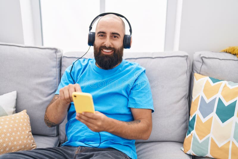 Young Bald Man Listening To Music Sitting On Sofa At Home Stock Image