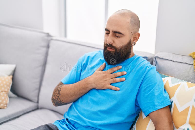 Young Bald Man Sitting on Sofa Suffering Heart Attack at Home Stock ...