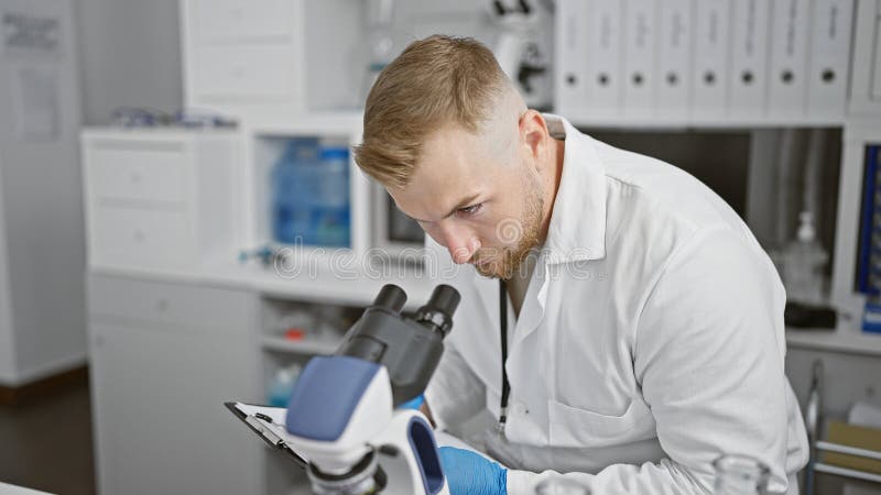 A Young Bearded Man in a Laboratory Observes a Microscope while Holding ...