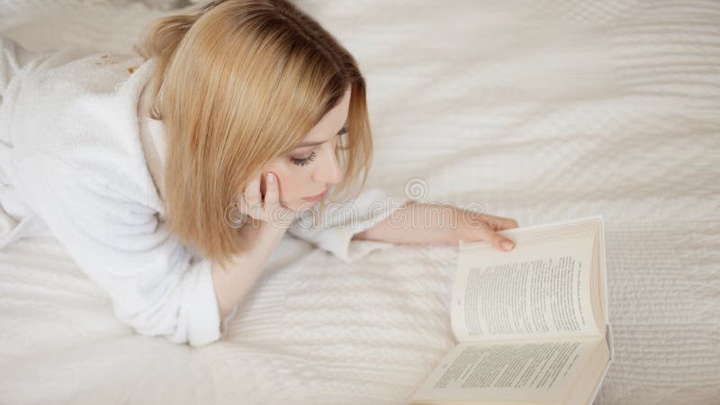 Young Beautiful Blonde Is Reading An Interesting Book In Her Bedroom