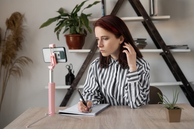 A Young Beautiful Caucasian Girl Sits at a Table Watching a Video ...