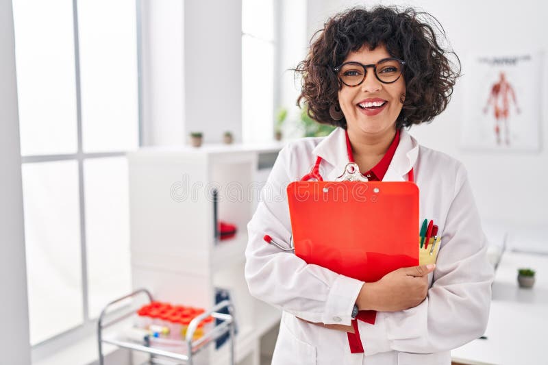 Young Beautiful Hispanic Woman Doctor Smiling Confident Holding ... Young Beautiful Hispanic Woman Doctor Smiling Confident Holding ...