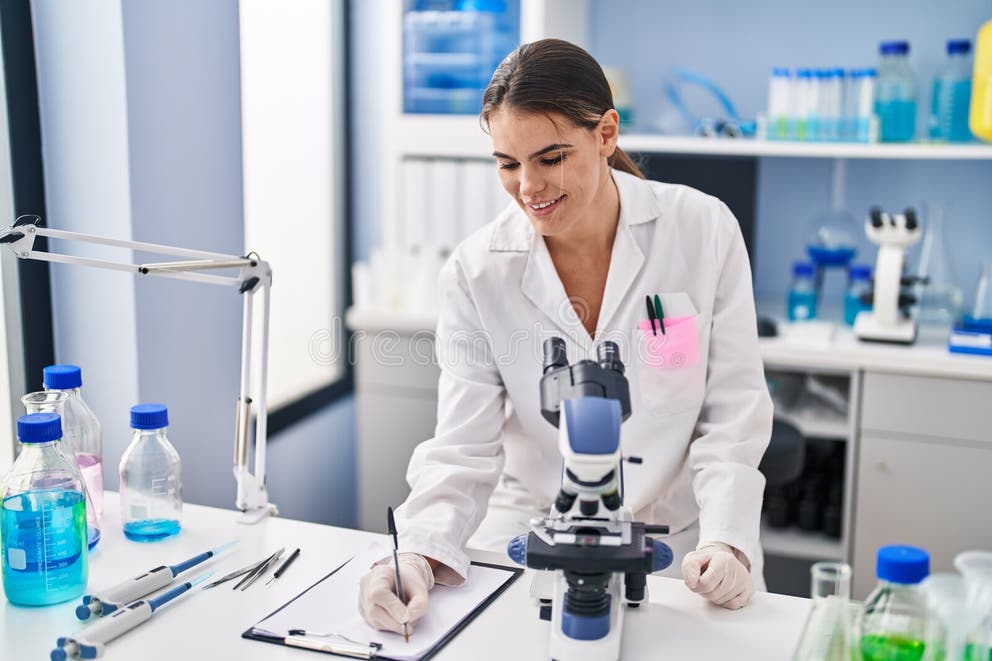 Young Beautiful Hispanic Woman Scientist Using Microscope Writing on ...