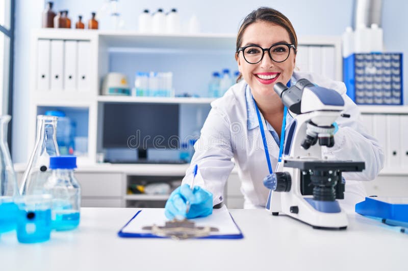Young Beautiful Hispanic Woman Scientist Using Microscope Writing on ...