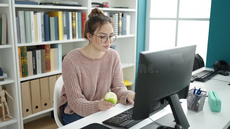 Young Beautiful Hispanic Woman Student Using Computer Eating Apple at ...