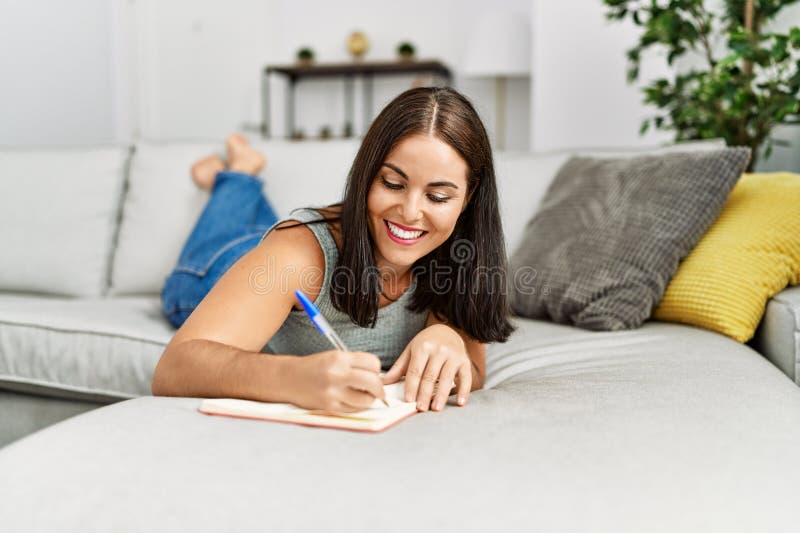 Young Beautiful Hispanic Woman Writing on Notebook Lying on Sofa at ...