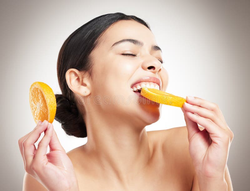 Young Beautiful Mixed Race Woman Eating An Orange While Posing Against