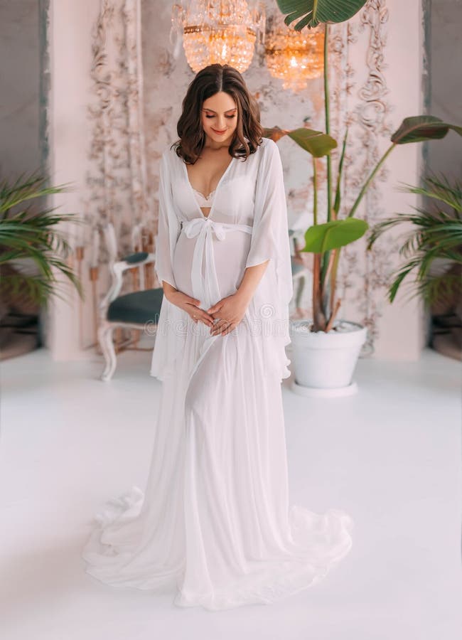 Young Beautiful Pregnant Woman Stand Near Window Hugs Bare Belly With