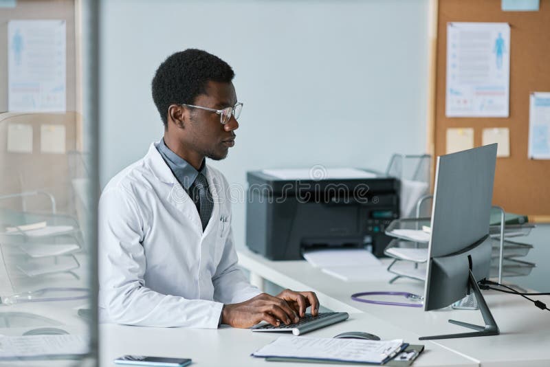Young Black Doctor Using Computer at Desk in Office Working in Clinic ...