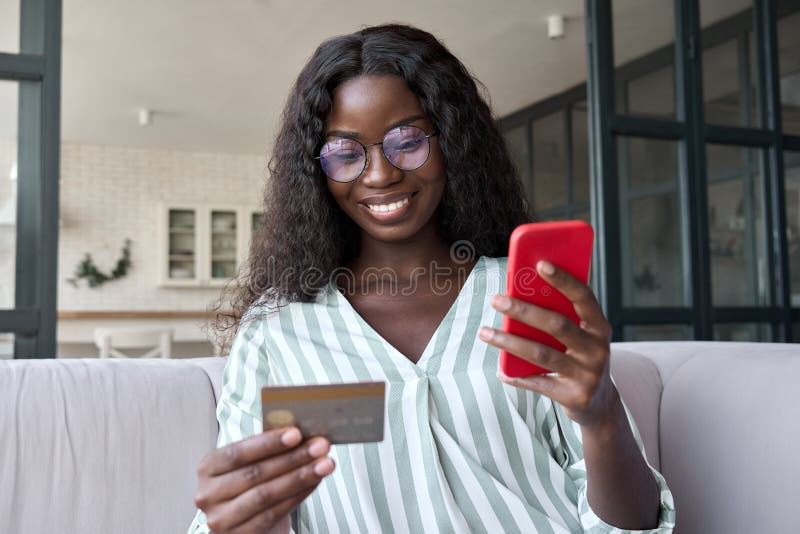 Young Black Smiling Woman Holding Credit Card Using Cell Phone at Home ... Young Black Smiling Woman Holding Credit Card Using Cell Phone at Home ...